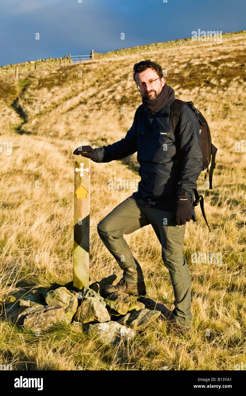 A walker leaning against a waymarker for the St Cuthbert's Way long ...