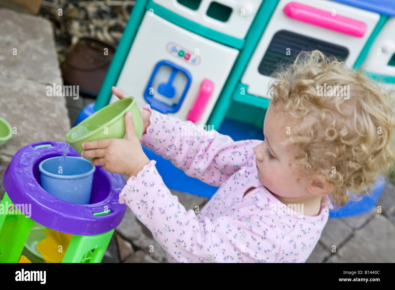 Toddler pouring water into water toy outdoors on patio on warm summer ...
