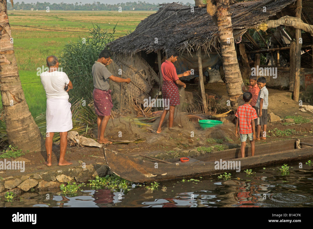Fisherman family mending nets alongside canal in the backwaters of ...