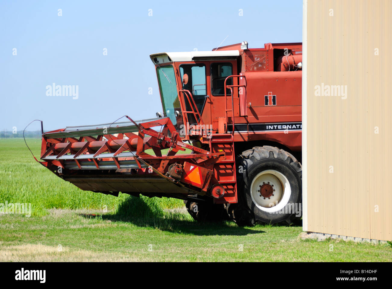A combine sits by an outbuilding and waits until harvest. A green wheat ...