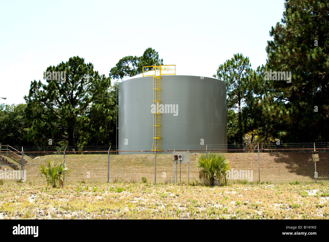 Large metal water tower with a yellow ladder surrounded by trees near ...