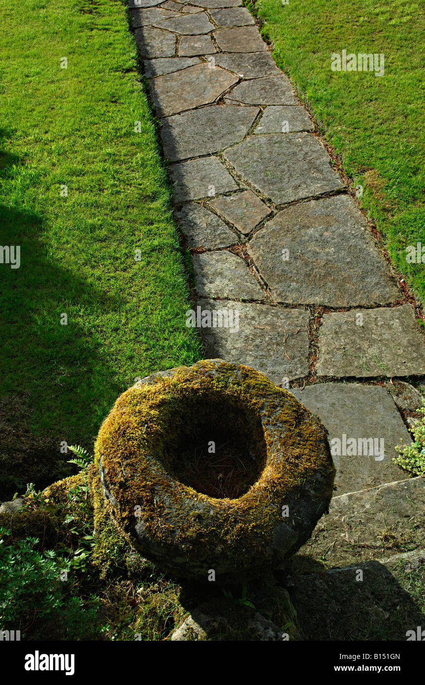 Moss covered stone urn against background of lawn and paved pathway in ...