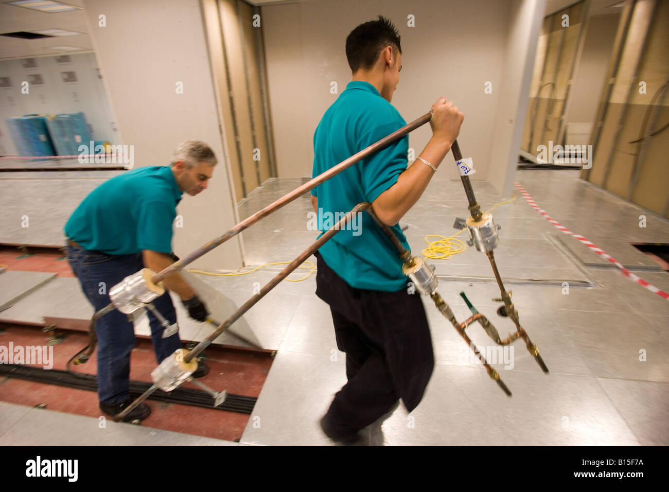 A workman carries a copper heating pip whilst another installed raised ...