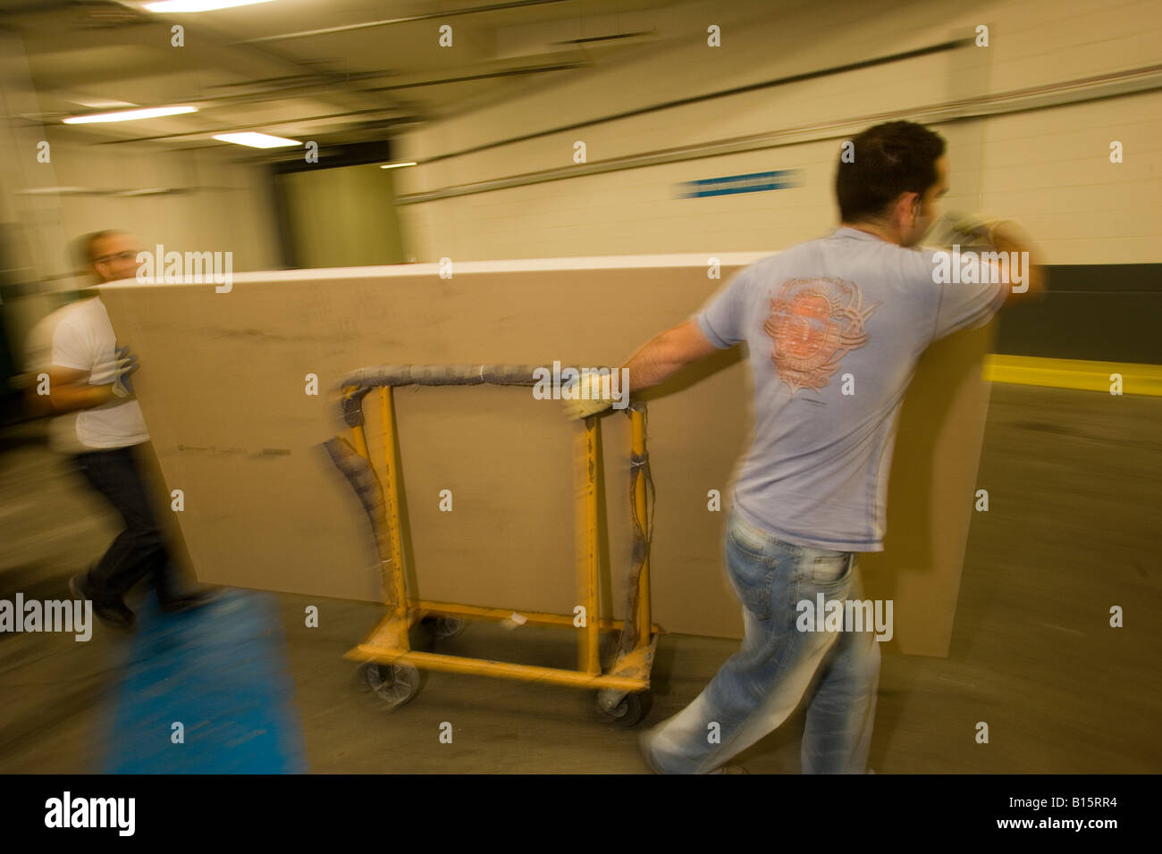 A pair of workmen move a sheets of plasterboard to the goods lift of an ...