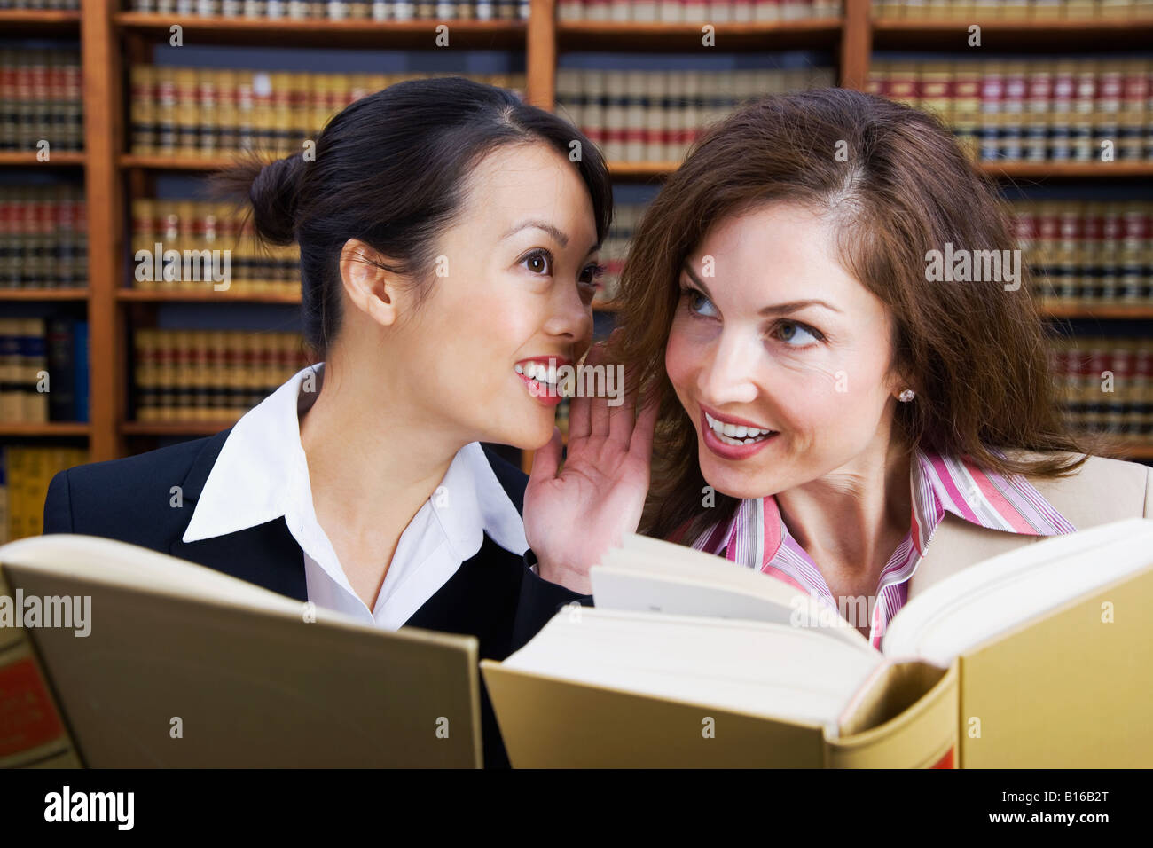 Multi-ethnic women whispering in law library Stock Photo - Alamy