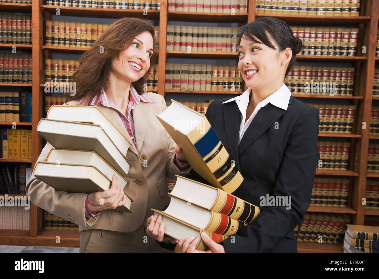 Multi-ethnic women carrying stacks of library reference books Stock ...
