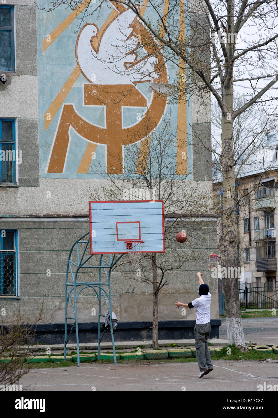 Boy playing basketball on court in old soviet era school with hammer ...