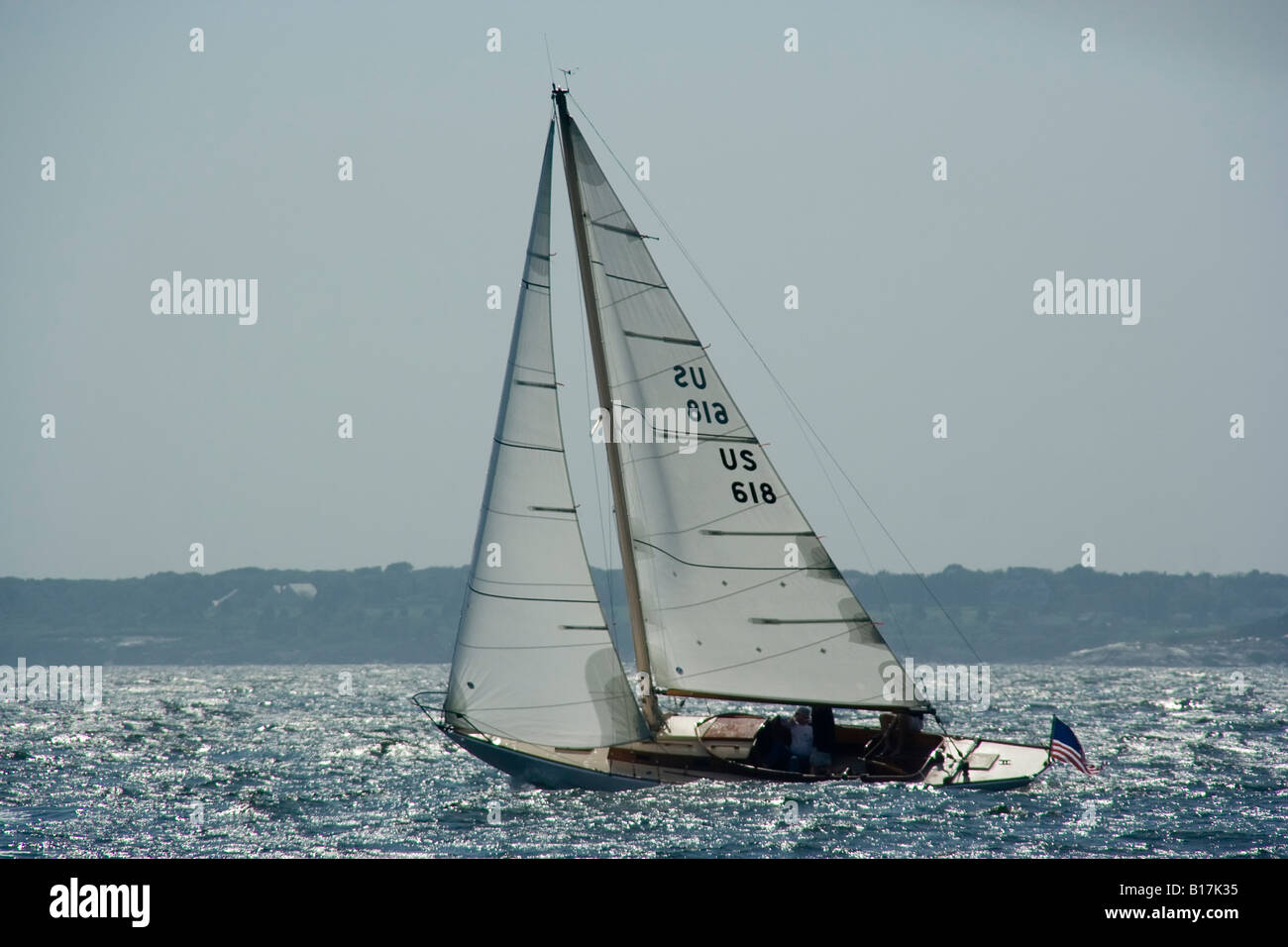 Photo of a classic sail boat sailing in open water with land in the ...