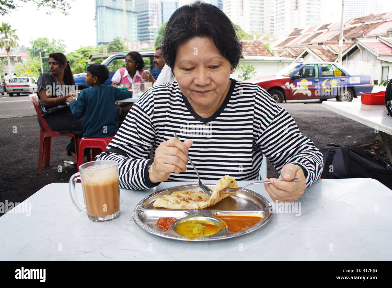 Chinese woman eating roti canai at outdoor food stall Stock Photo - Alamy