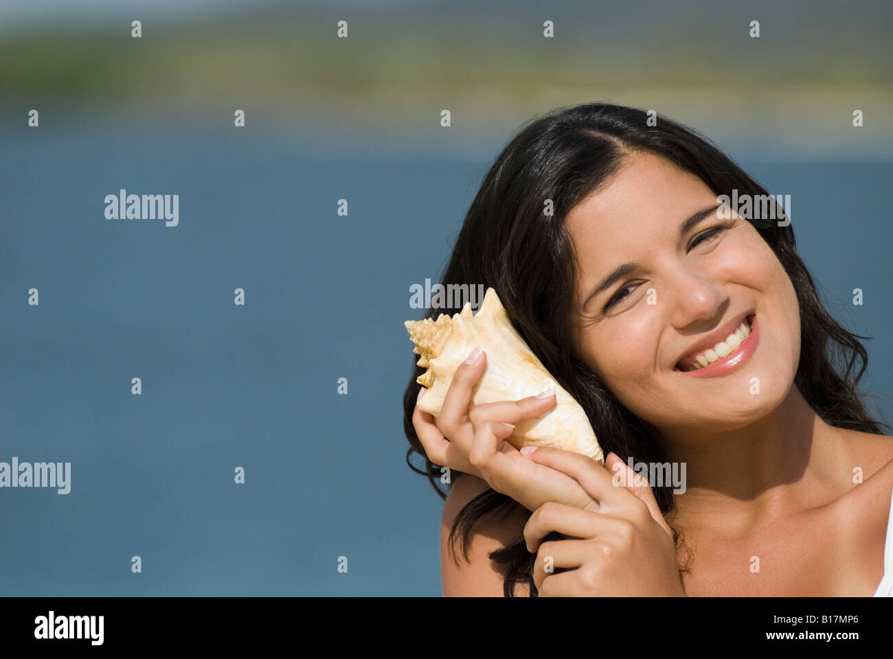 Hispanic woman listening to seashell Stock Photo - Alamy
