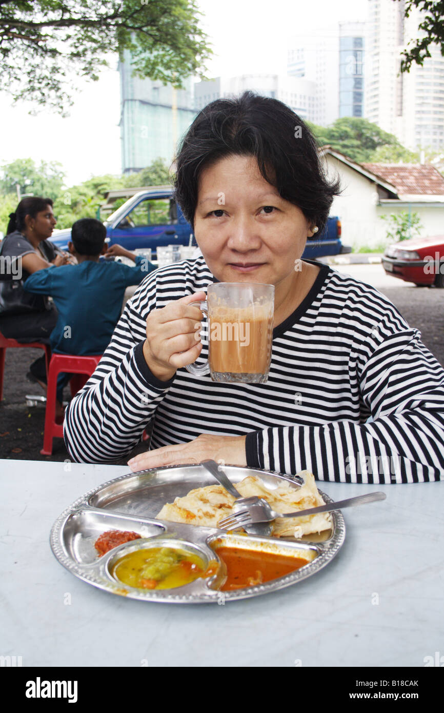 Chinese woman having meal of roti canai and drinking tea Stock Photo ...