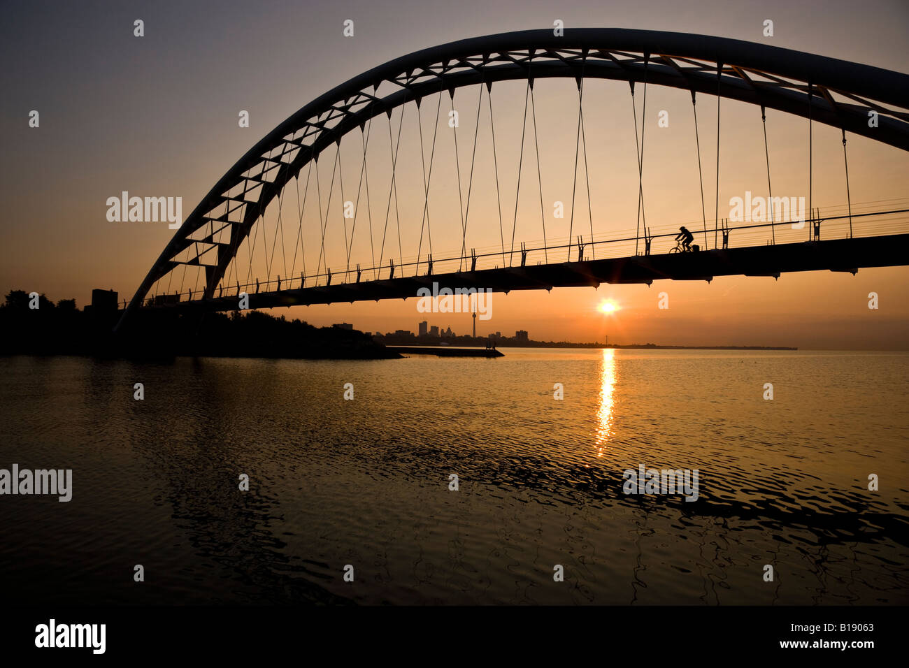 Cyclist crosses Humber River Pedestrian Bridge at sunrise with Toronto ...