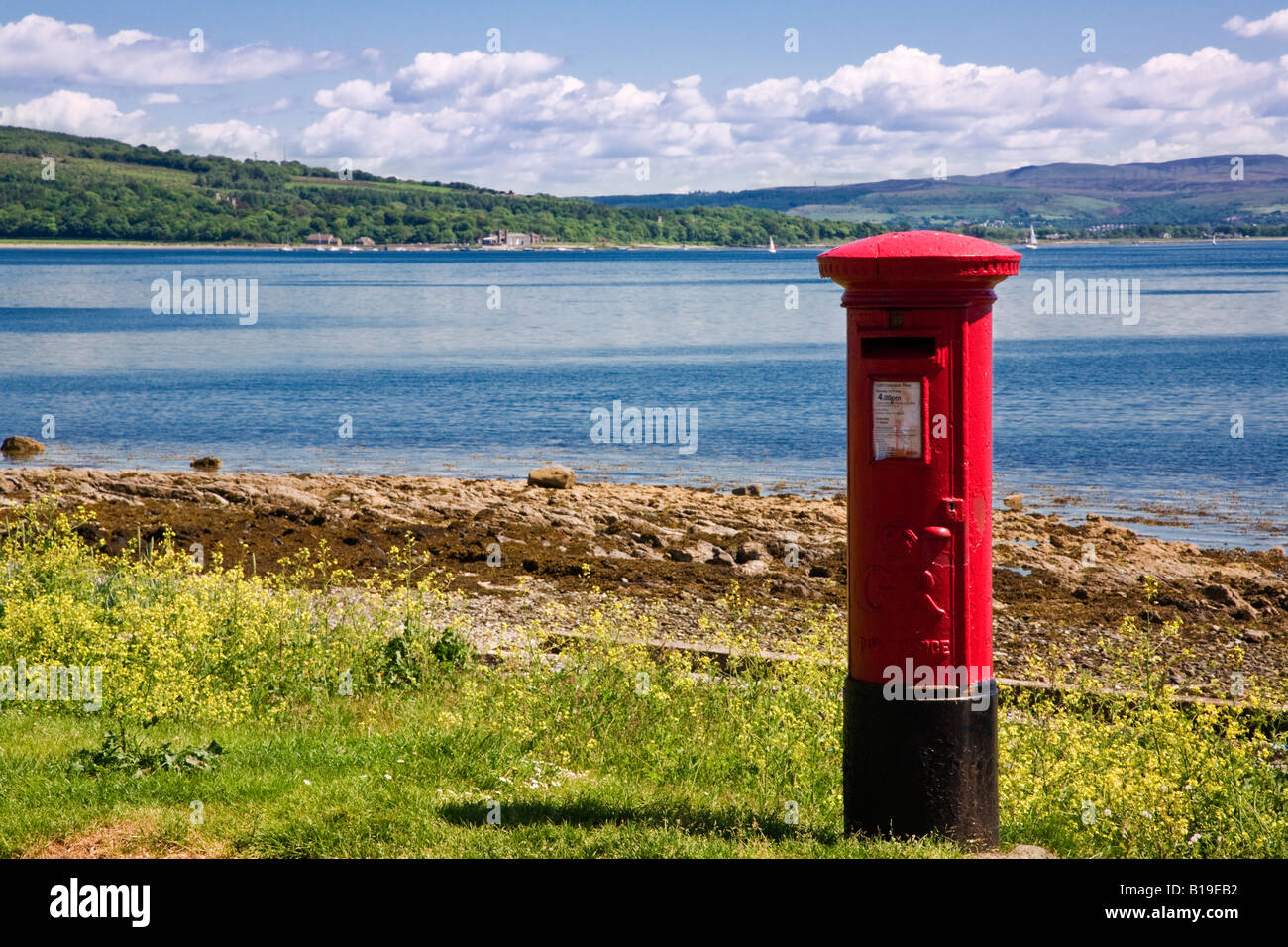 A red Royal Mail pillar box standing on the shoreline at Port Bannatyne ...