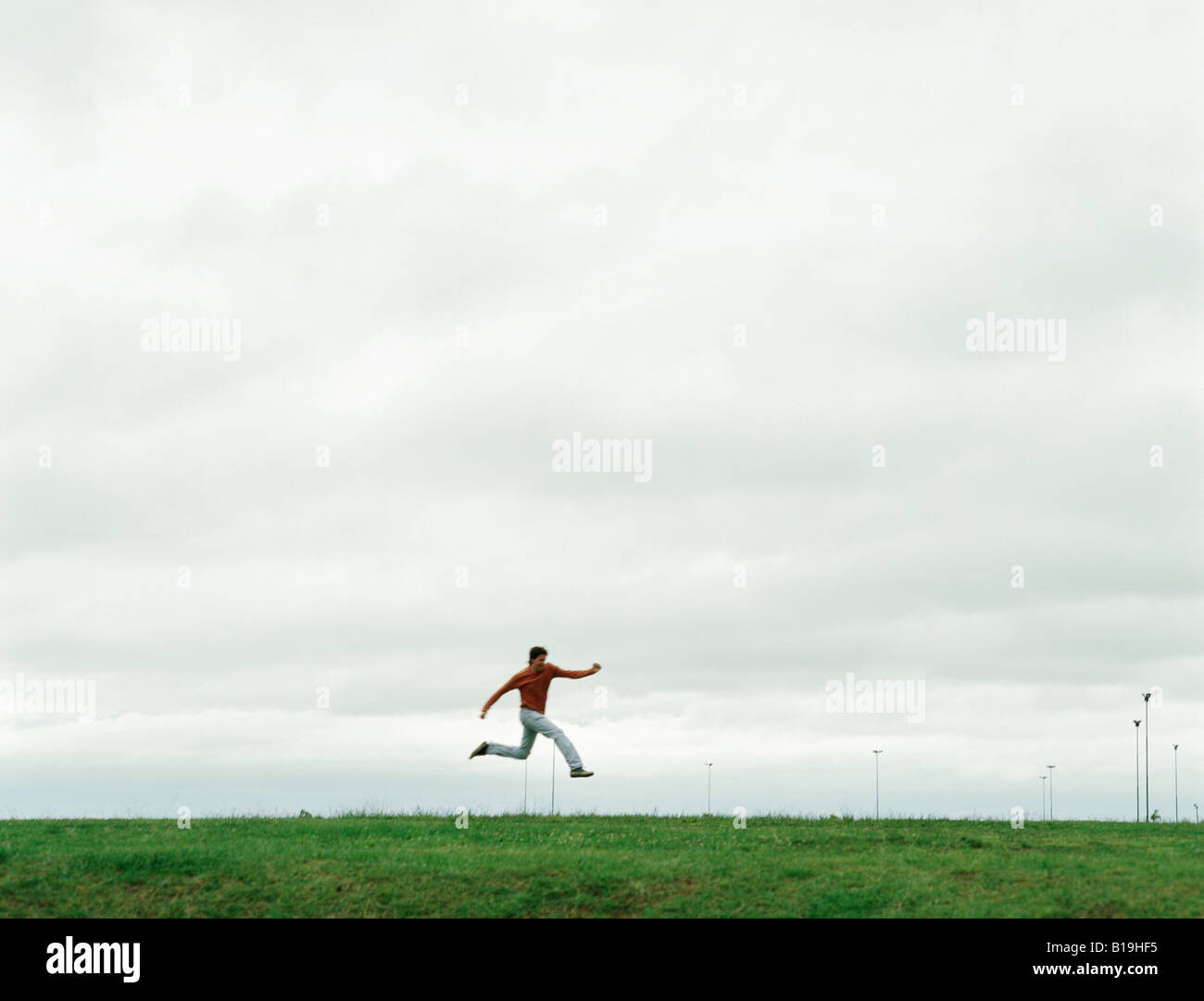 Man jumping on grassy field, in the distance Stock Photo - Alamy