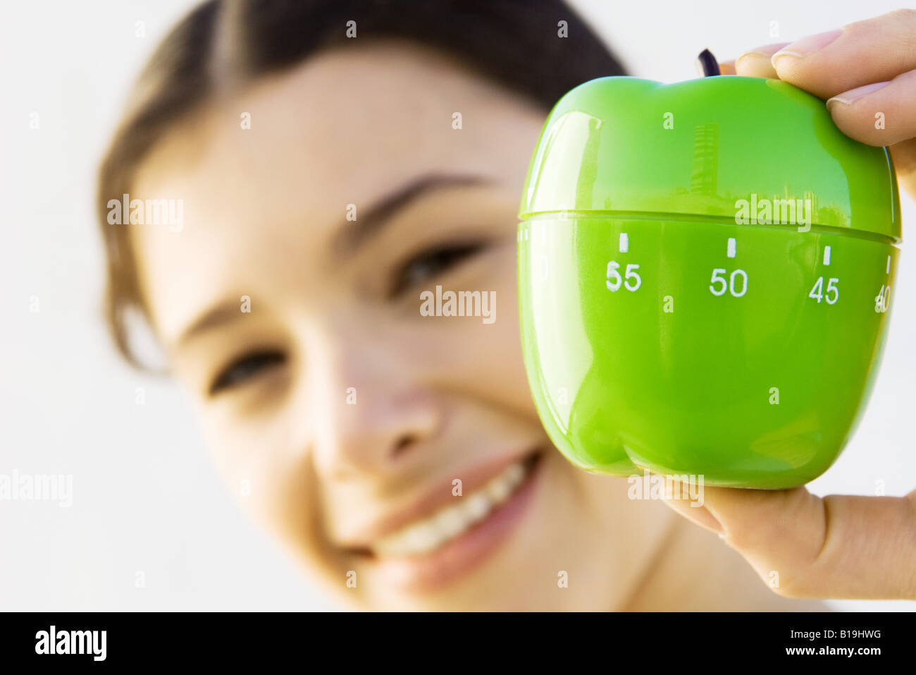 Woman holding up kitchen timer, smiling at camera, focus on foreground ...