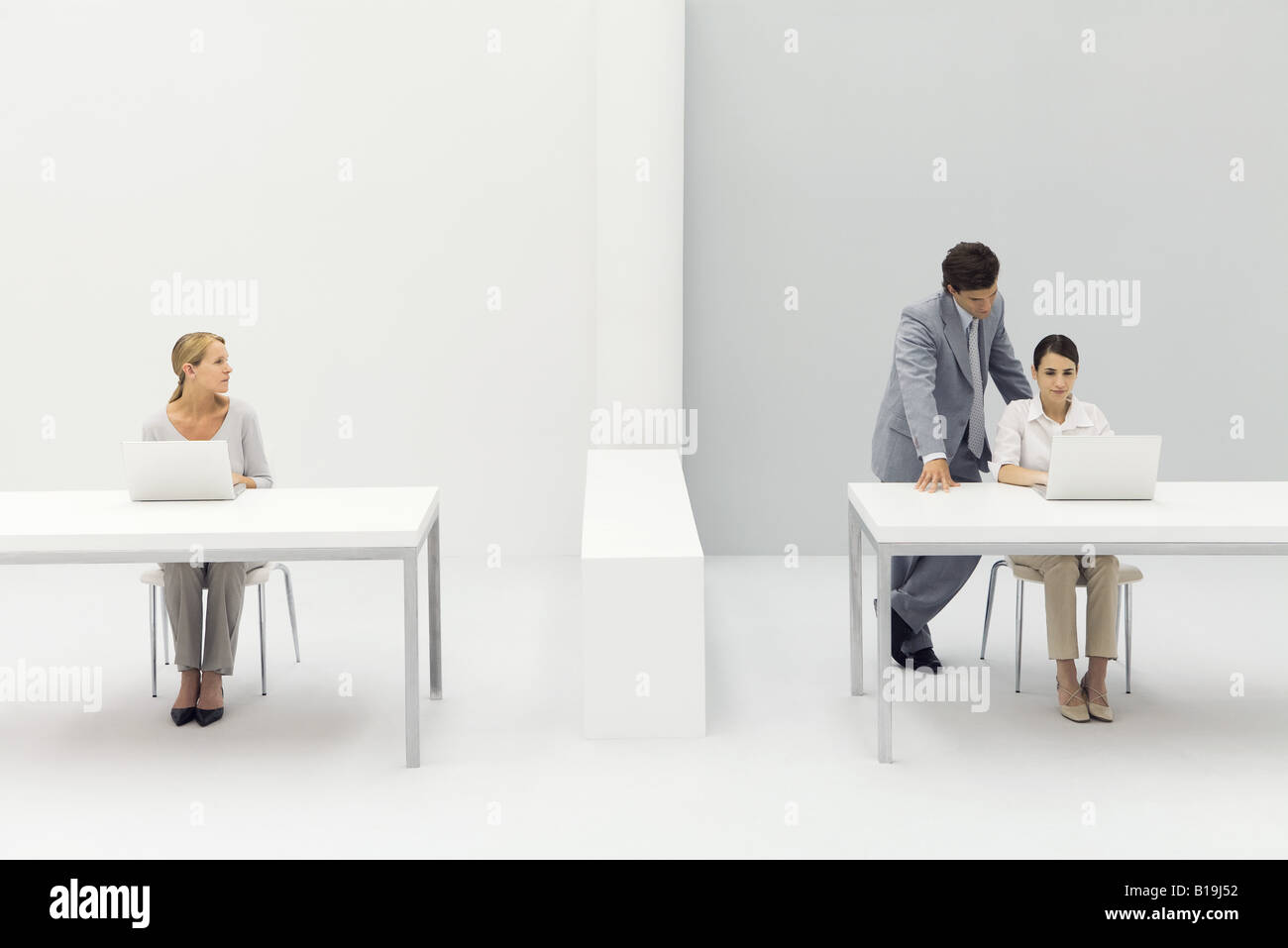Two women working in office, man standing behind one with his hand on ...