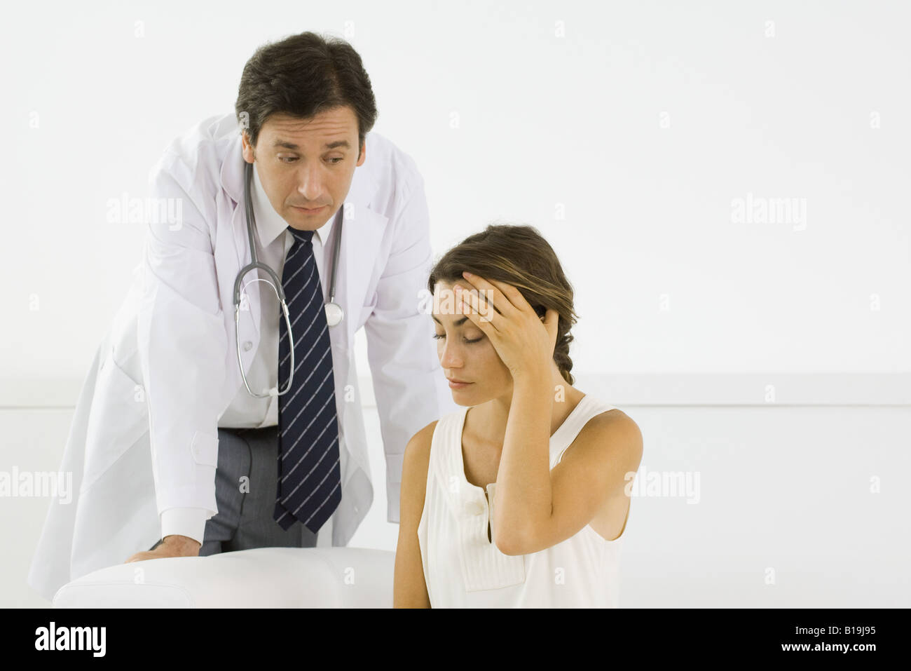 Woman holding head, doctor leaning behind her Stock Photo - Alamy