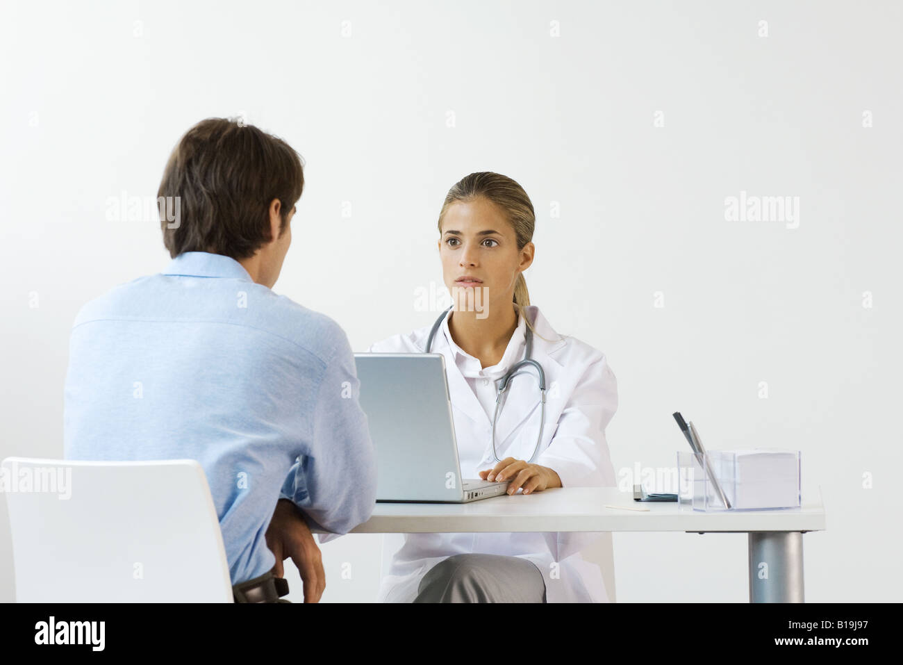 Female doctor sitting across from male patient at desk, using laptop ...