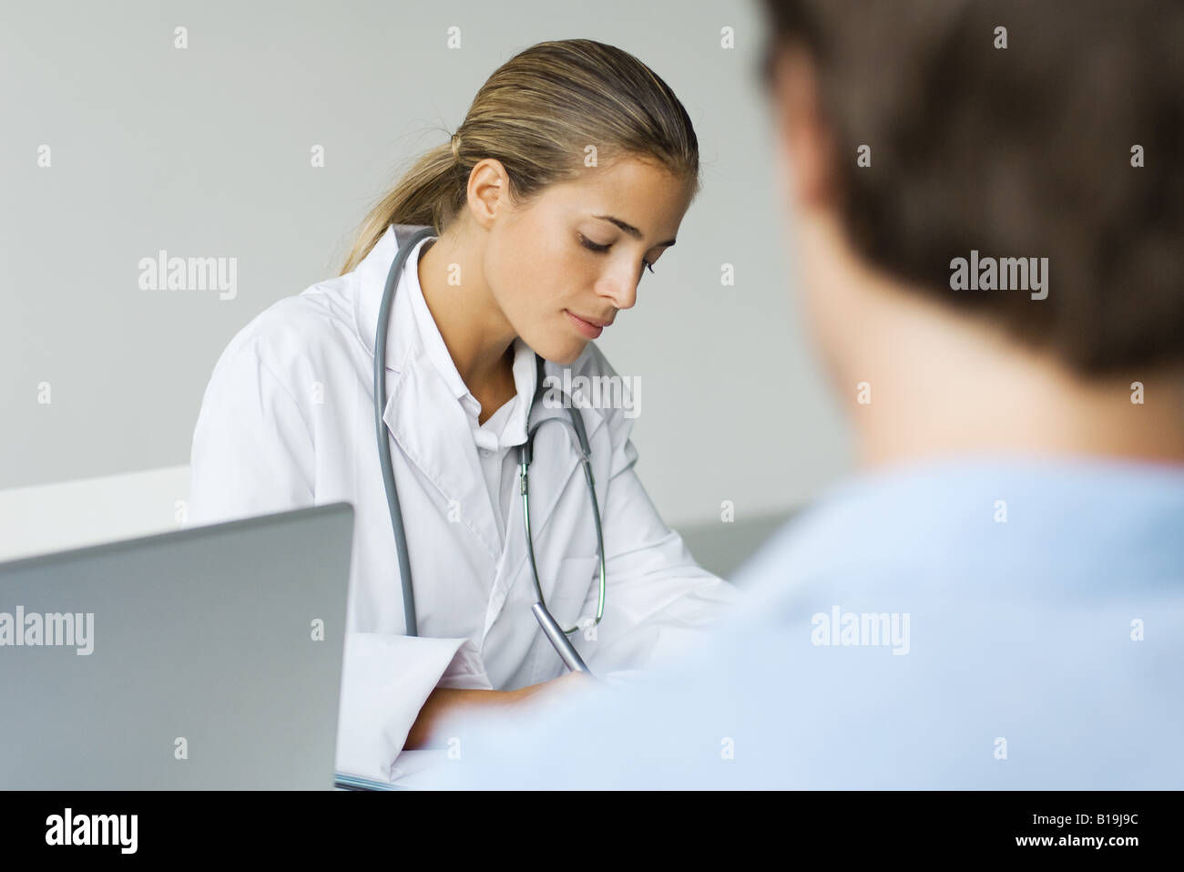 Doctor writing at desk, patient in foreground Stock Photo - Alamy