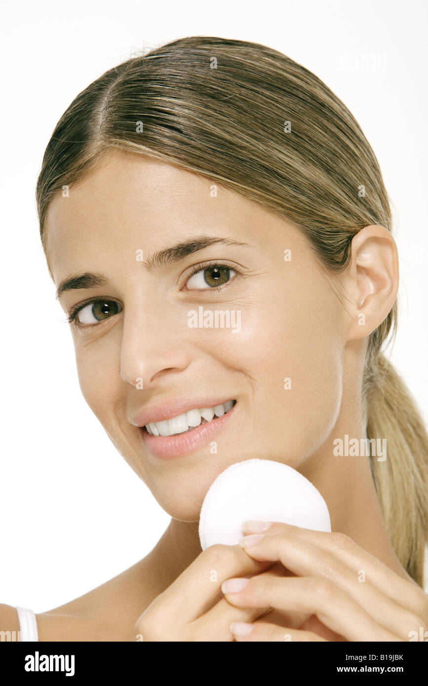 Woman using powder puff on cheek, smiling at camera Stock Photo - Alamy