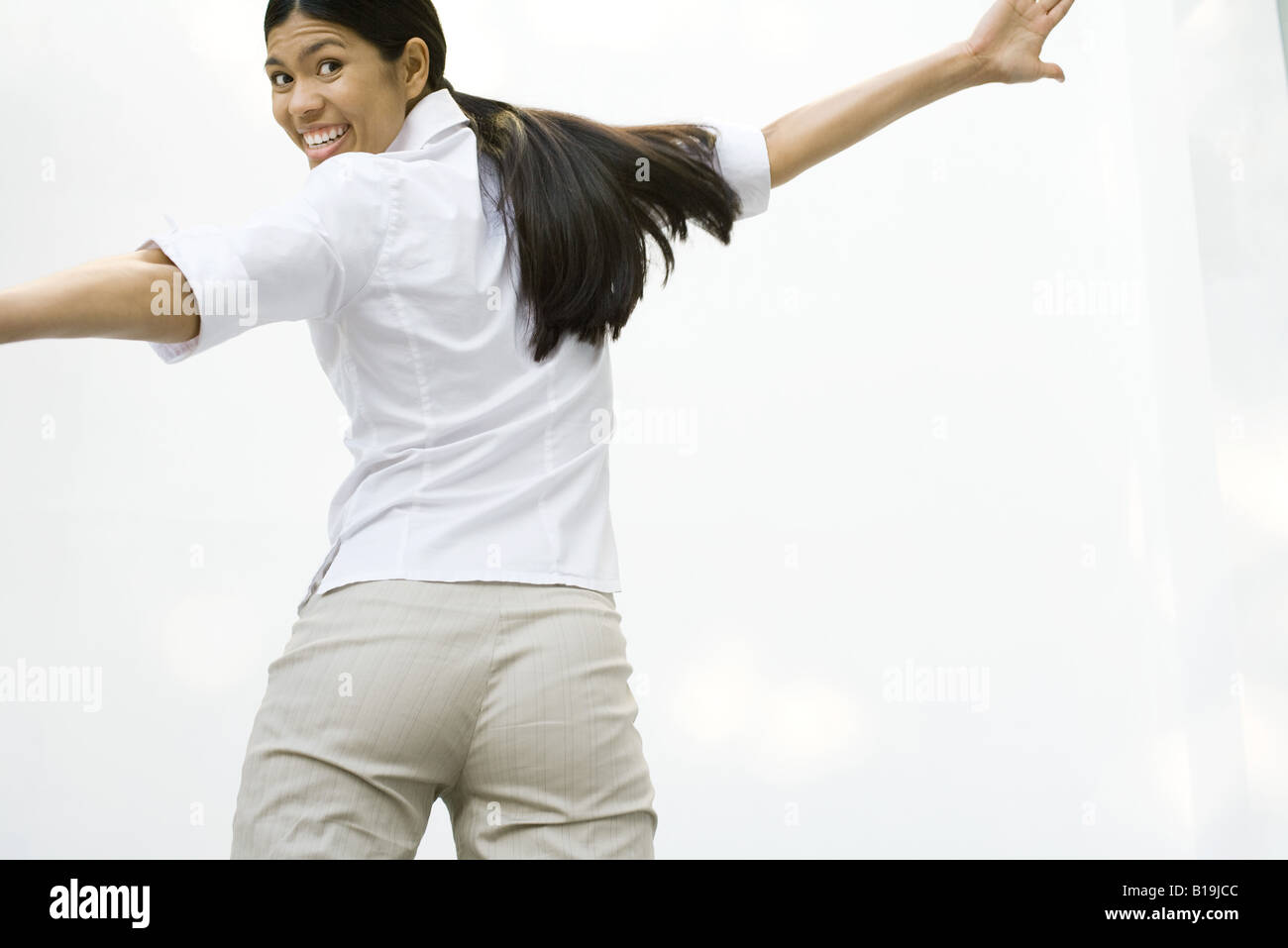 Woman smiling over shoulder at camera, arms spread, rear view Stock ...