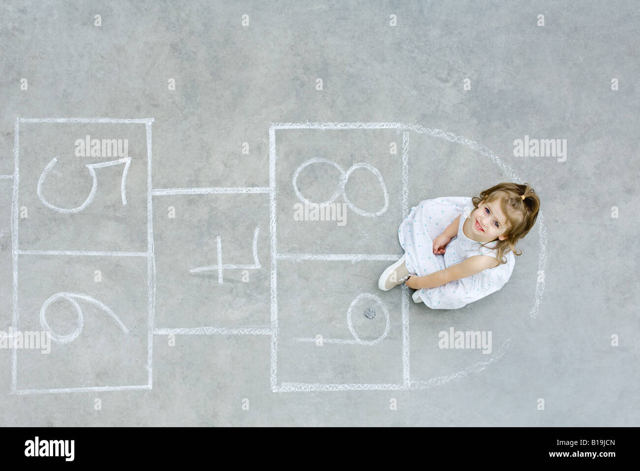 Girl sitting down on hopscotch grid, looking up, overhead view Stock ...