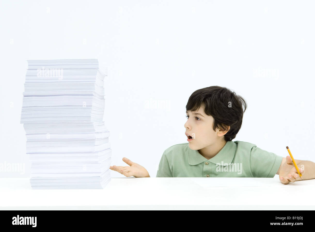 Boy looking at tall stack of paper, shrugging in disbelief, holding ...