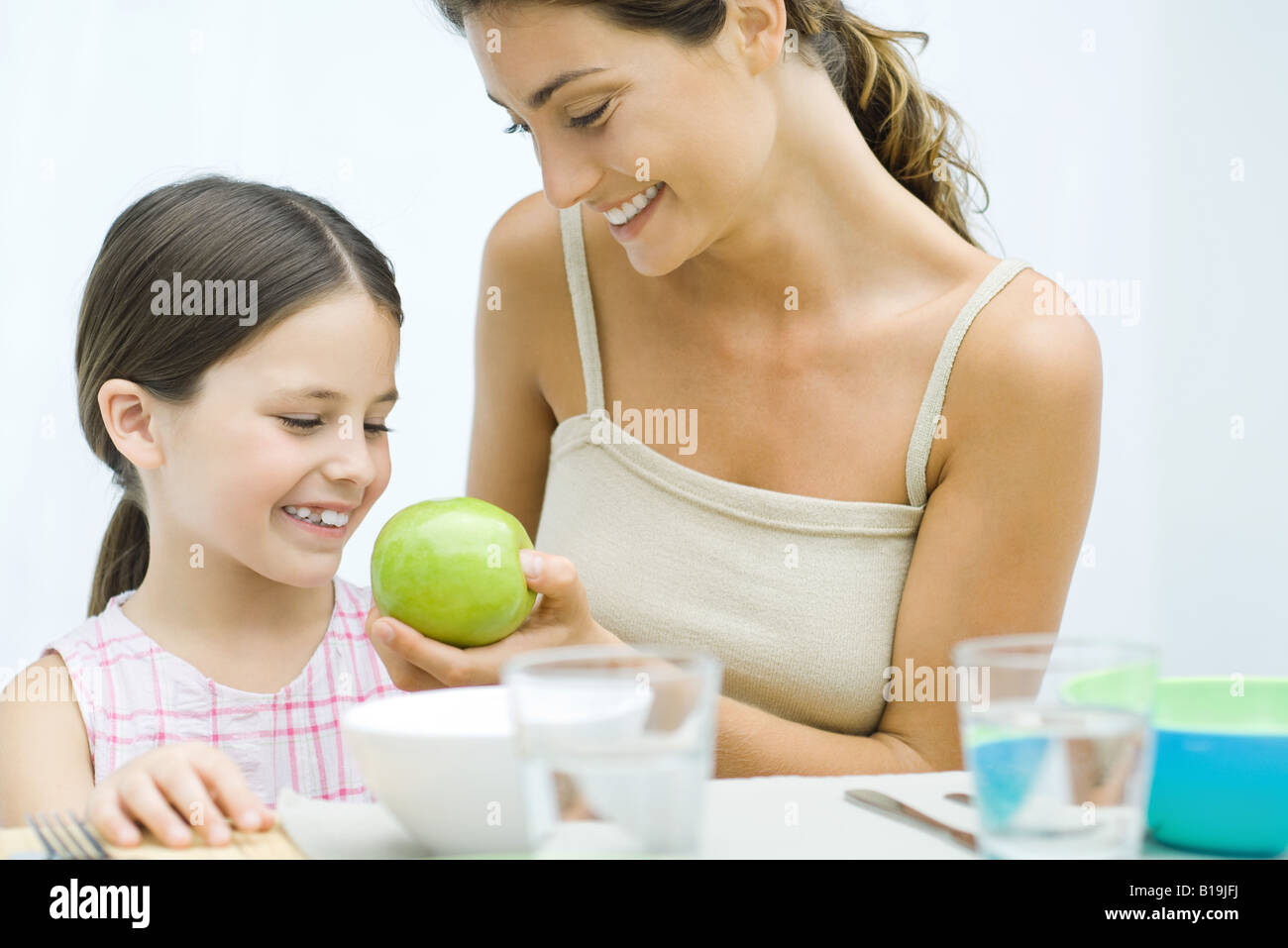 Mother giving daughter an apple, both smiling Stock Photo - Alamy
