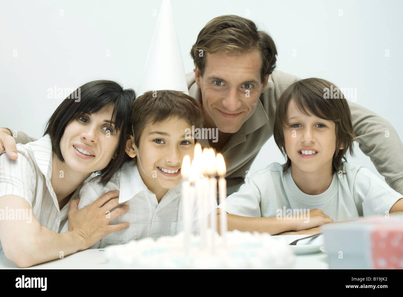 Family in front of birthday cake with lit candles, one boy wearing ...