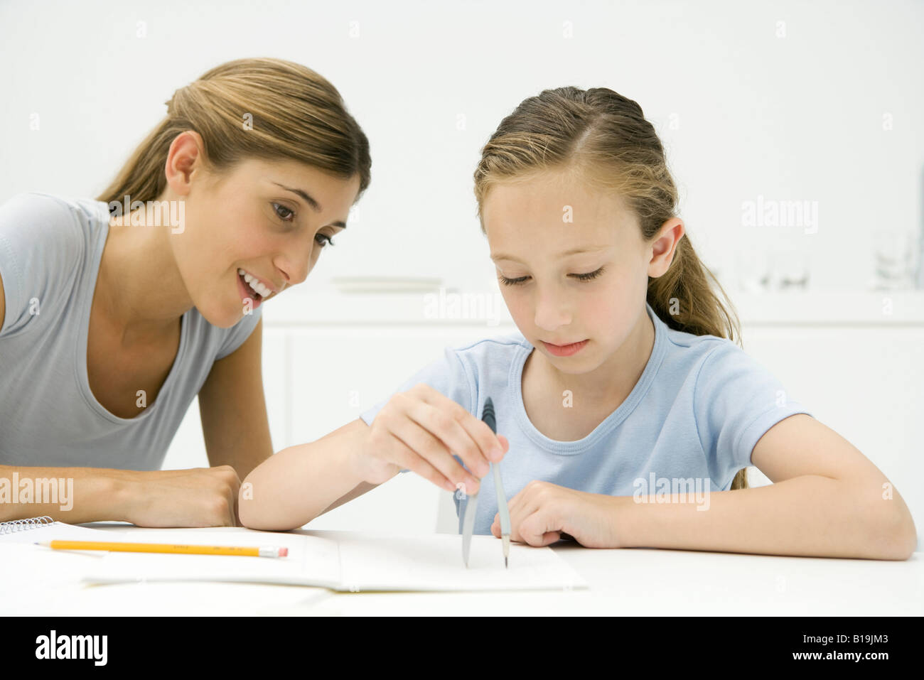 Girl doing homework, using drawing compass, mother watching Stock Photo ...