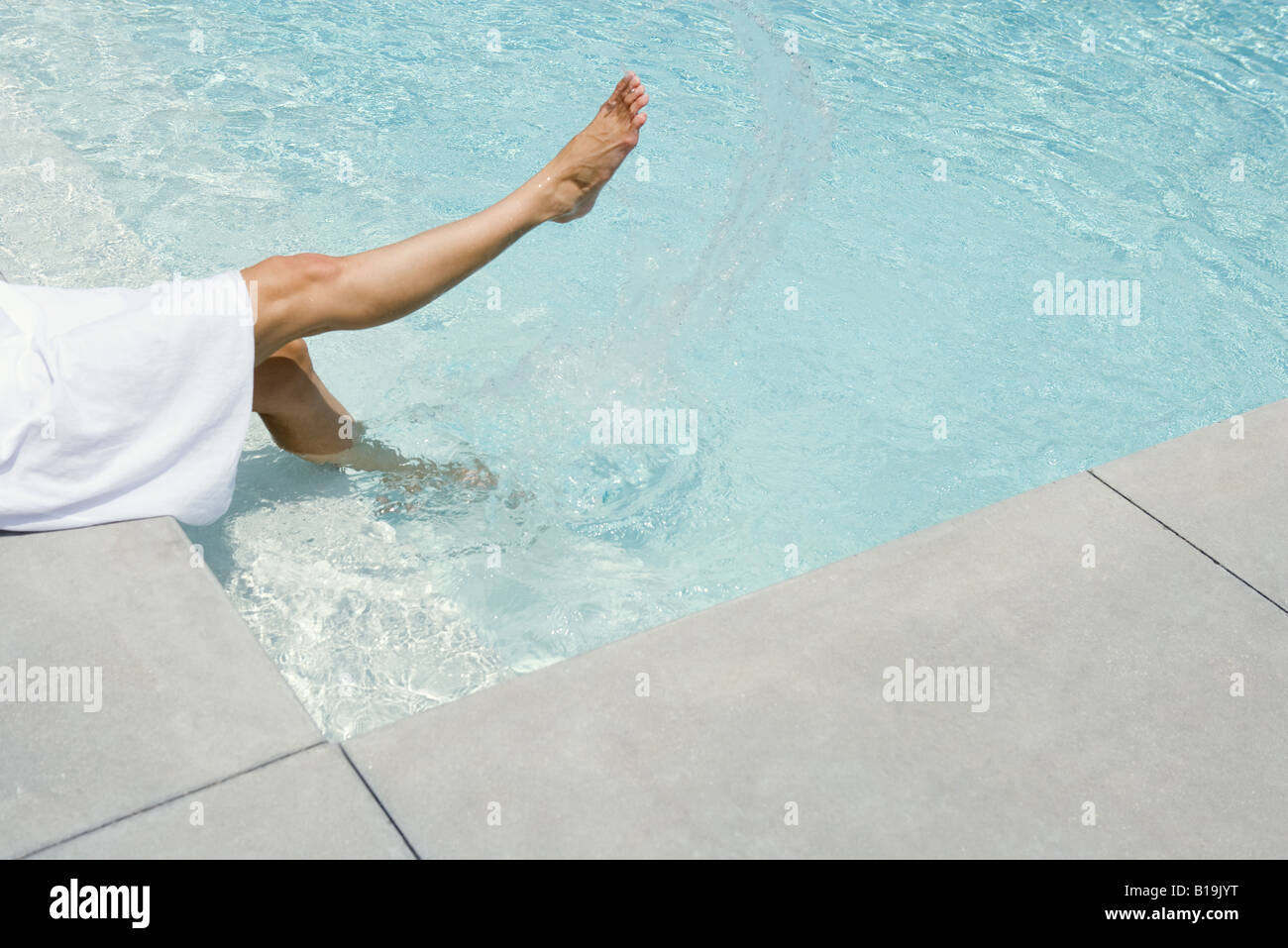 Woman sitting beside swimming pool, splashing water with feet, cropped ...