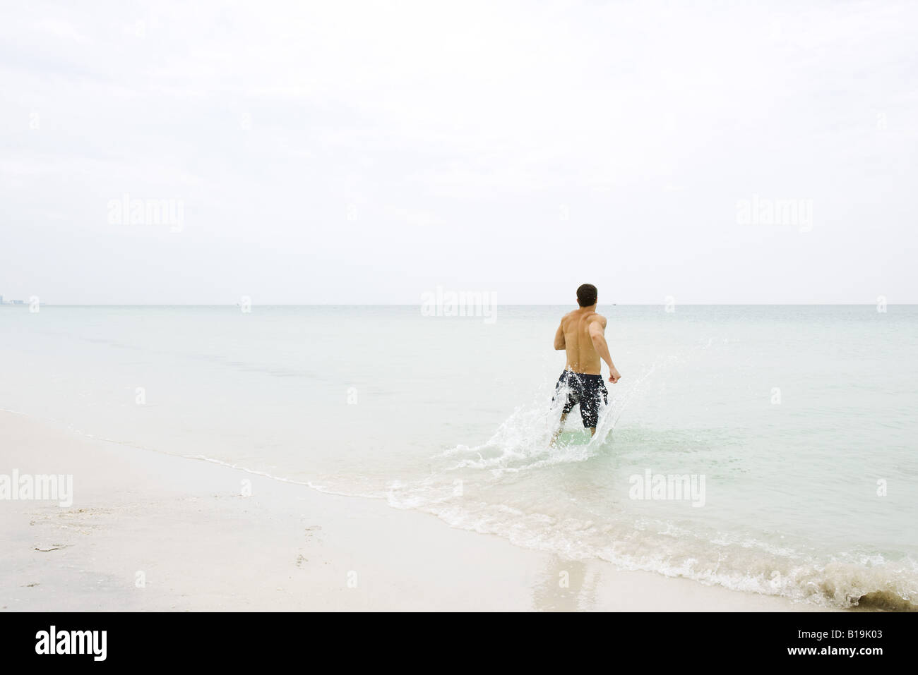Man running in shallow water at the beach, rear view Stock Photo - Alamy