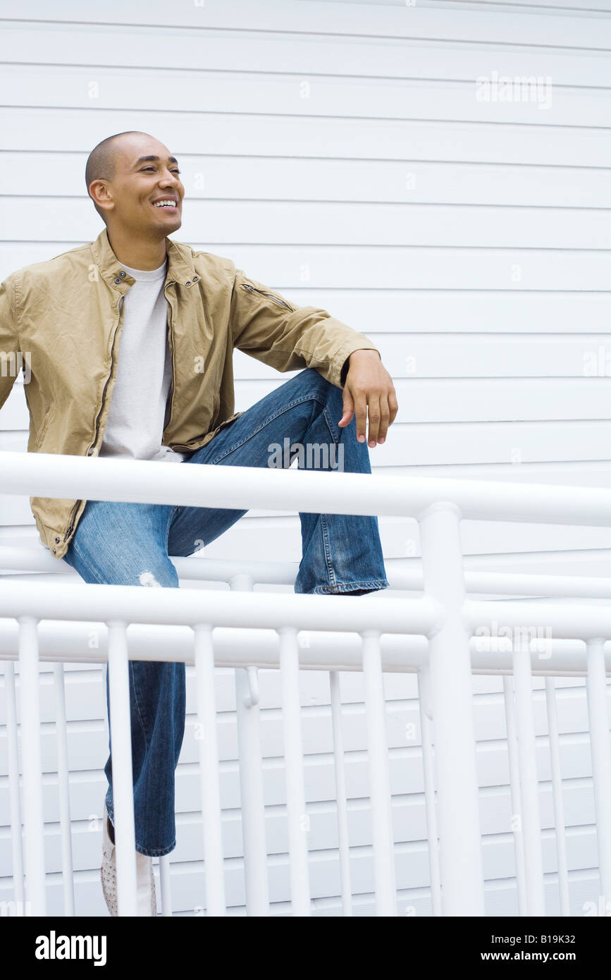 Man sitting on railing, looking away, smiling Stock Photo - Alamy