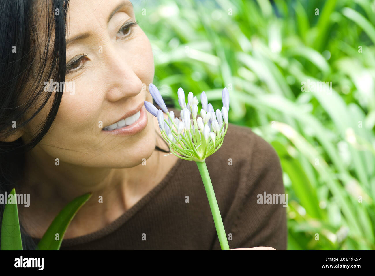Woman smelling African lily, smiling, looking away Stock Photo - Alamy