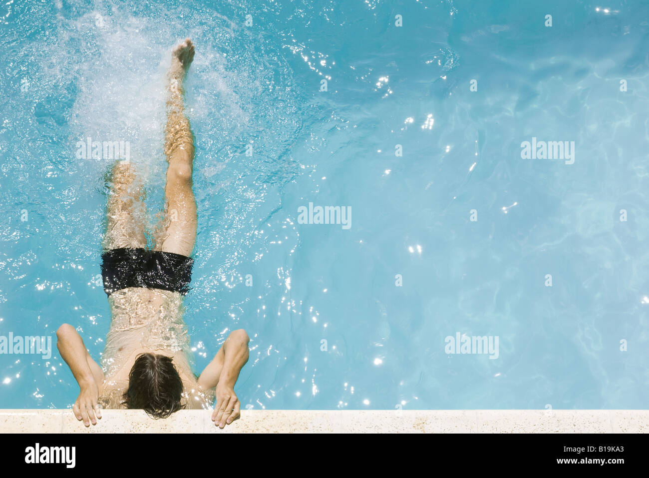 Man holding on to edge of swimming pool, kicking legs, high angle view ...