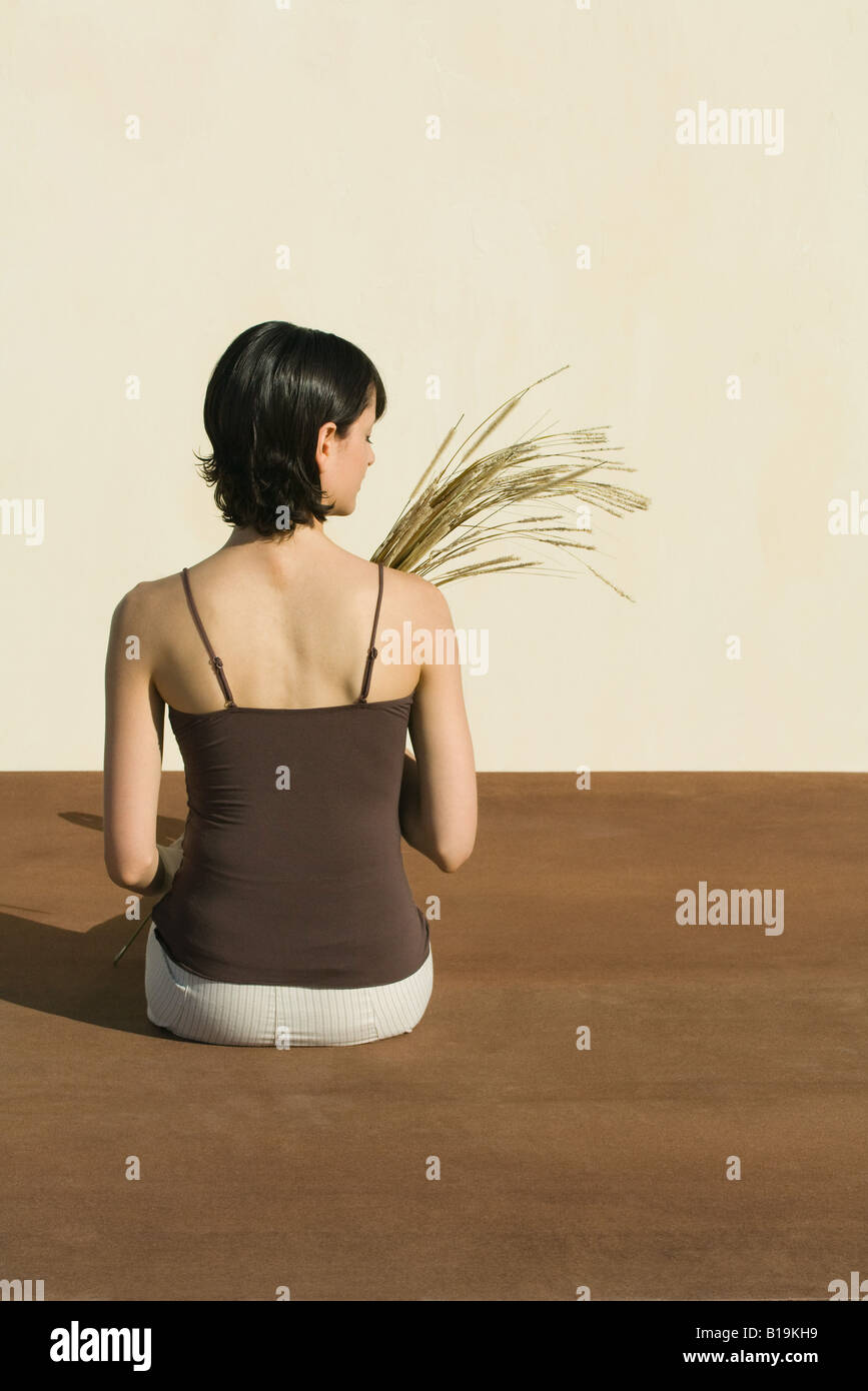 Woman sitting on the ground, holding wheat, rear view Stock Photo - Alamy