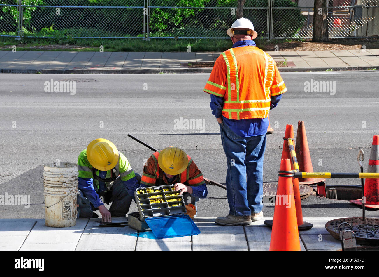 Utility workers prepare to work on and enter man hole in a city street ...