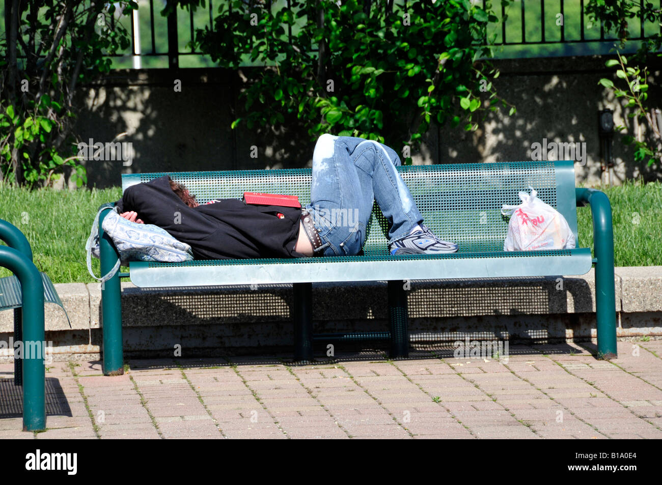 Homeless female woman laying on a city bench Stock Photo - Alamy