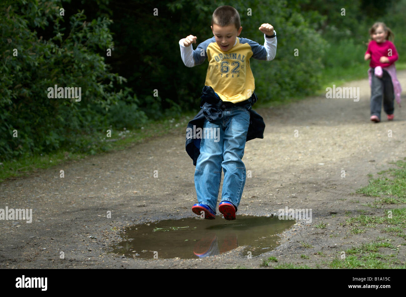 Young boy jumps into a puddle watched by his little sister Stock Photo ...