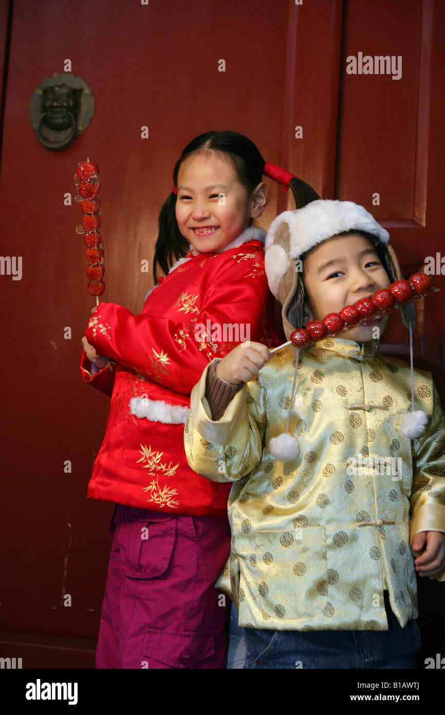 two chinese children dressed in traditional clothing eating candied ...