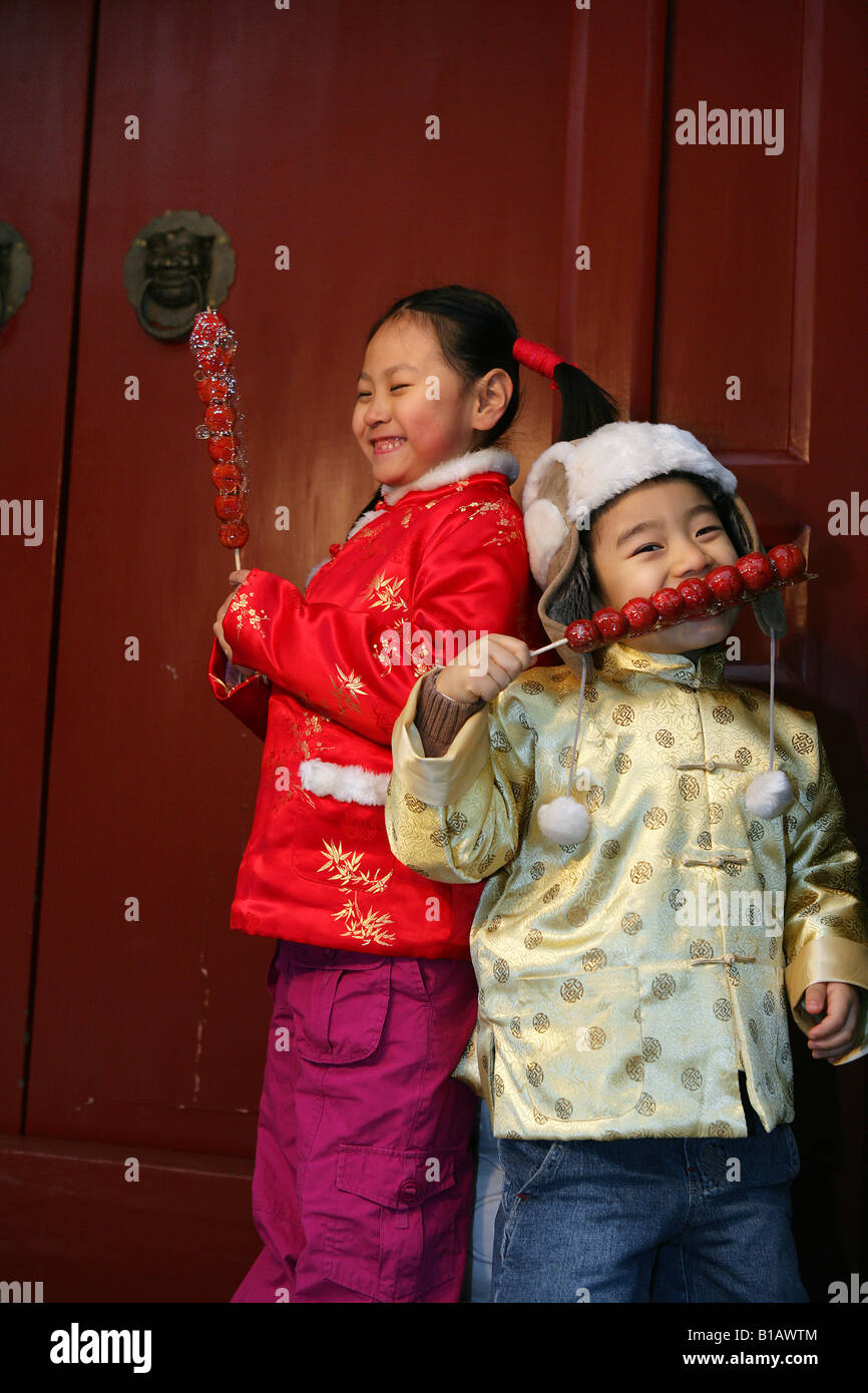 two chinese children dressed in traditional clothing eating candied ...