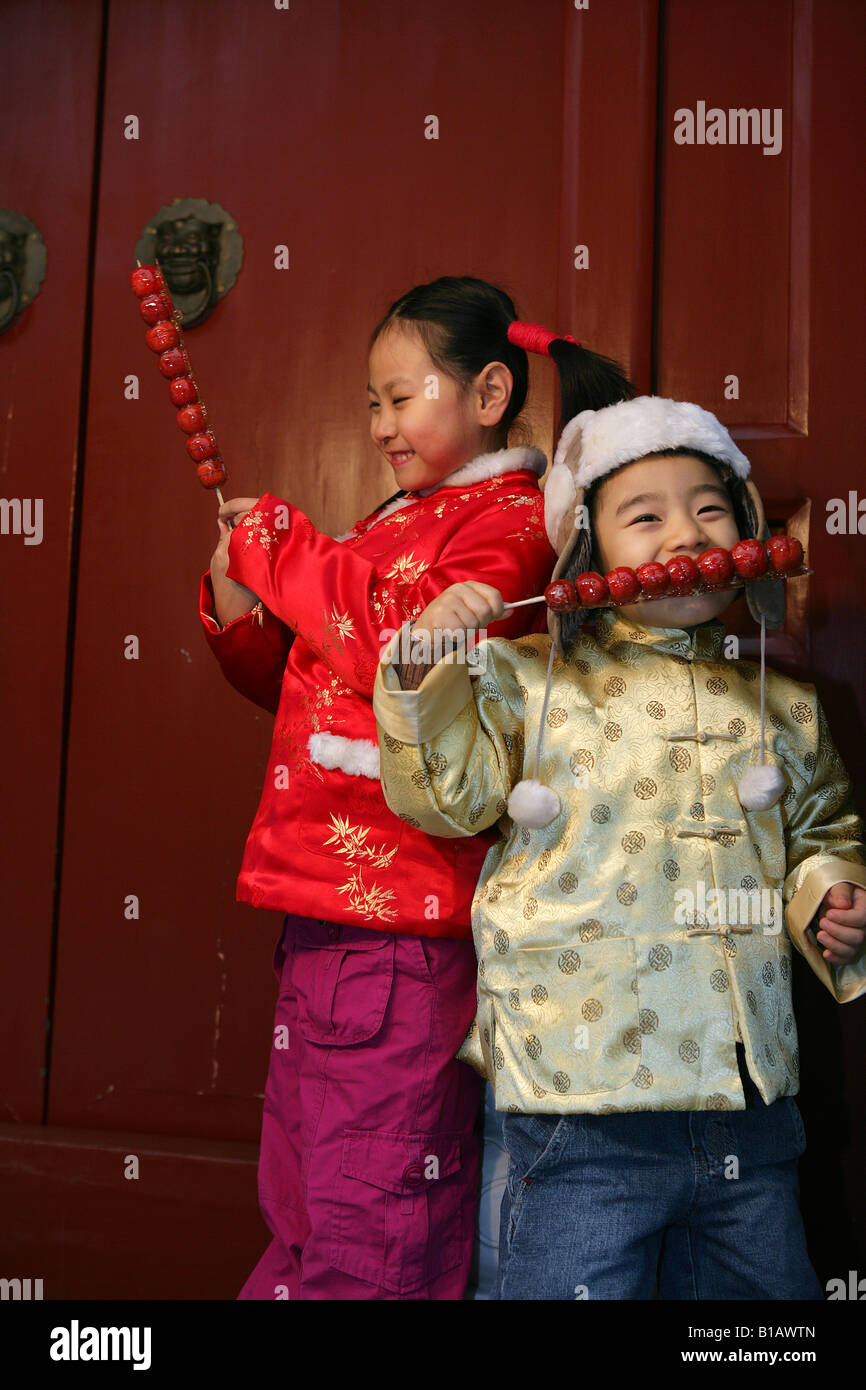 two chinese children dressed in traditional clothing eating candied ...
