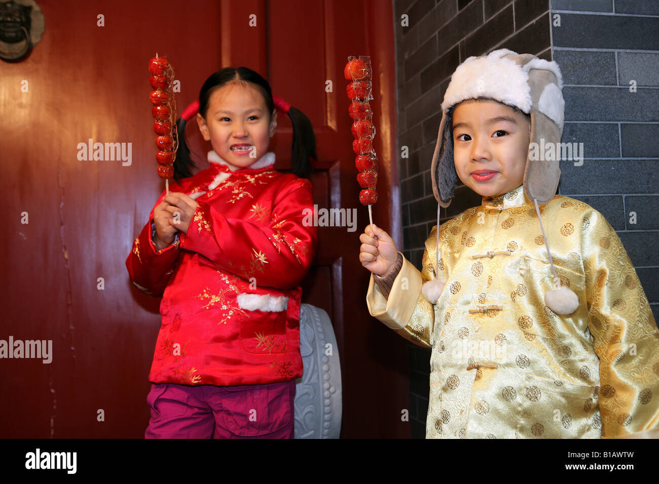 two chinese children dressed in traditional clothing raising candied ...