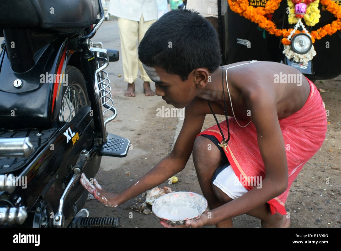 Young Hindu priest marks a motorcycle with a sandalwood substitute ...