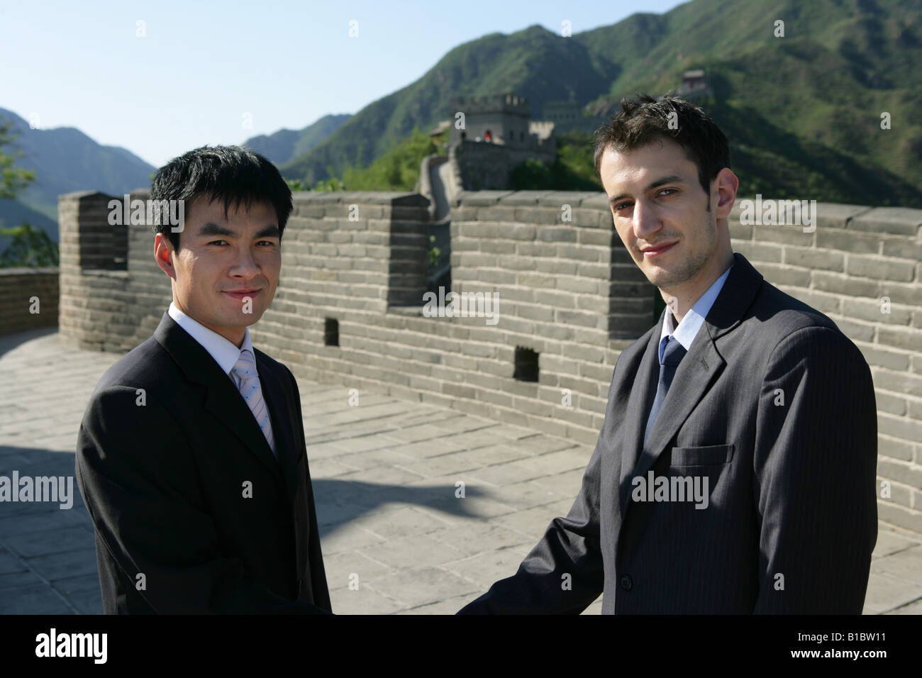 caucasian businessman and Chinese businessman handshaking on Great Wall ...