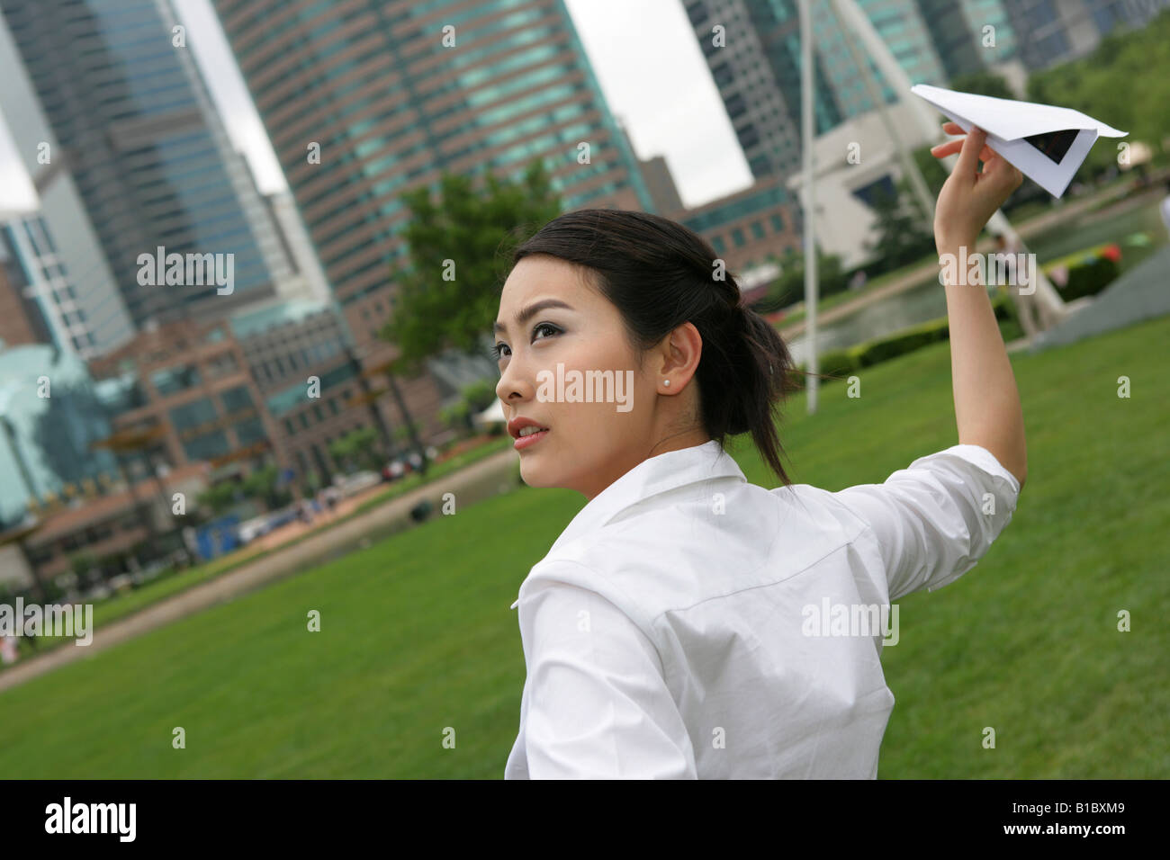 one businesswoman playing paper airplane on the lawn outside office ...