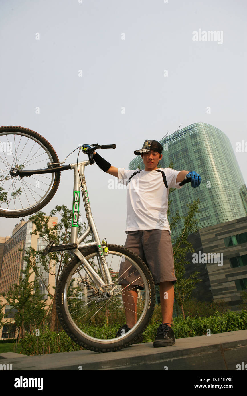 young man performing a stunt with a bicycle on square beside office ...