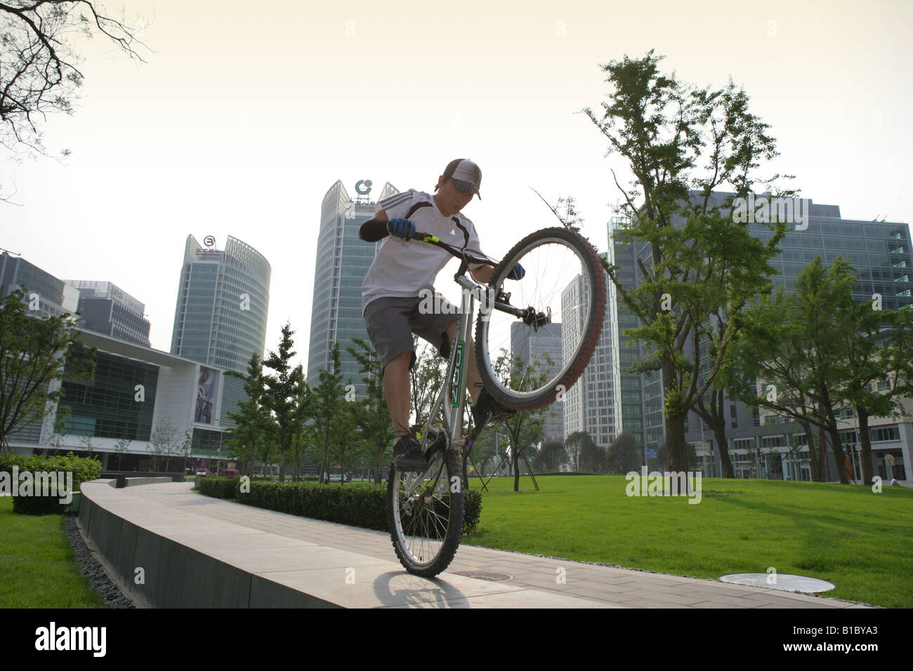 young man performing a stunt with a bicycle on square beside office ...