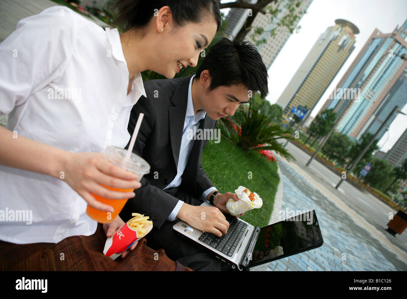 one businessman and one businesswoman eating fast-food while using ...