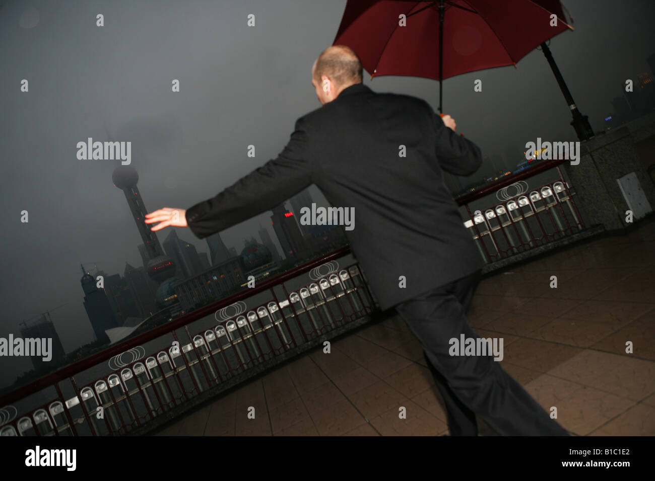 one foreign businessman jumping with an opened umbrella at the Bund ...